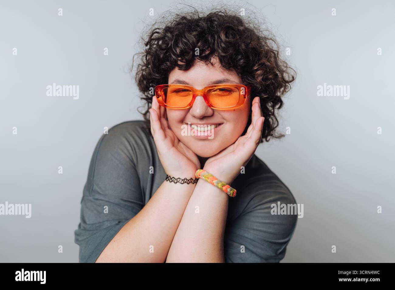 A cheerful person with curly hair wearing orange sunglasses poses ...
