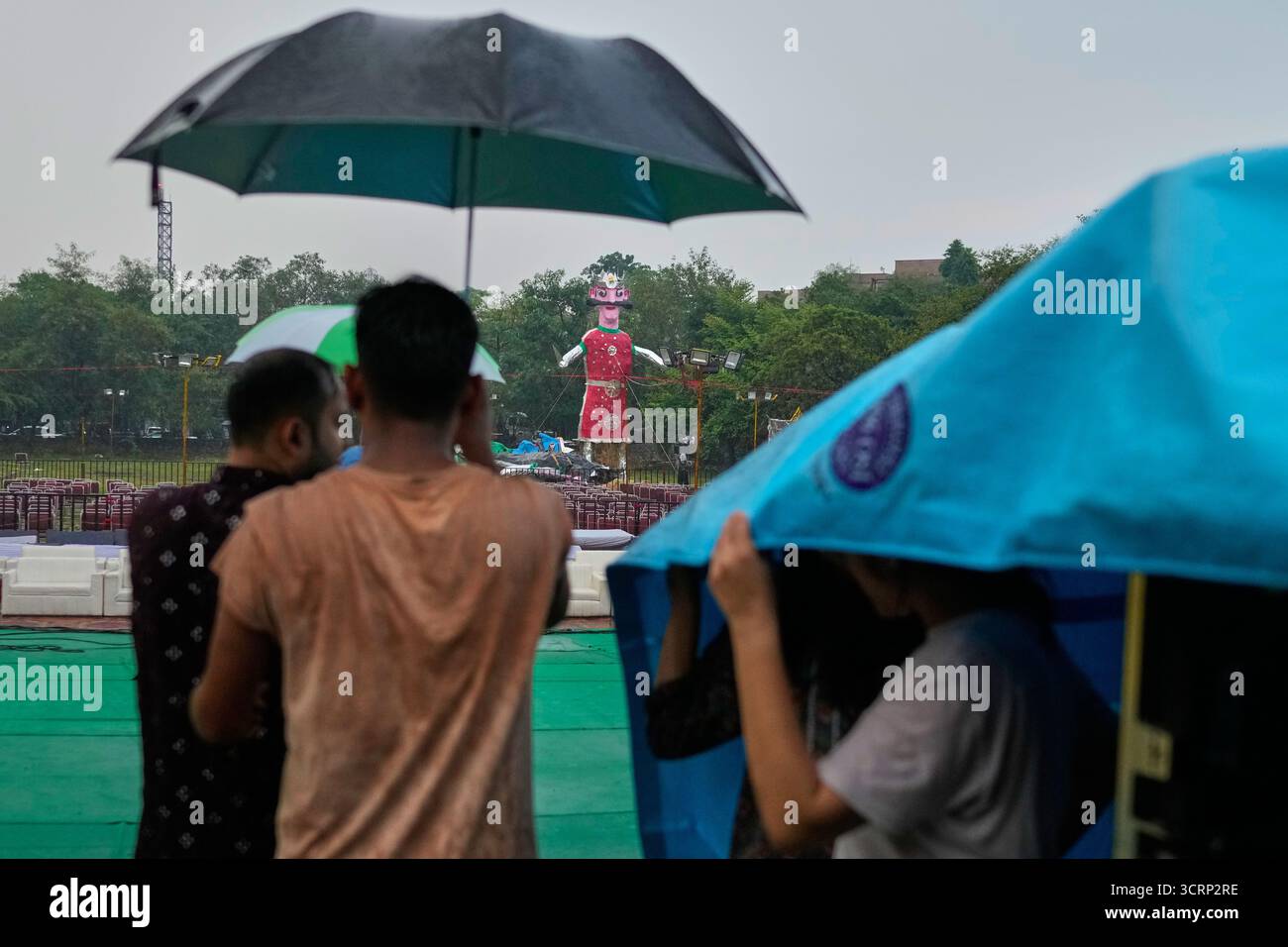 Organizers shelter under umbrellas and plastic sheeting as a sudden rain and thunderstorm causes ...