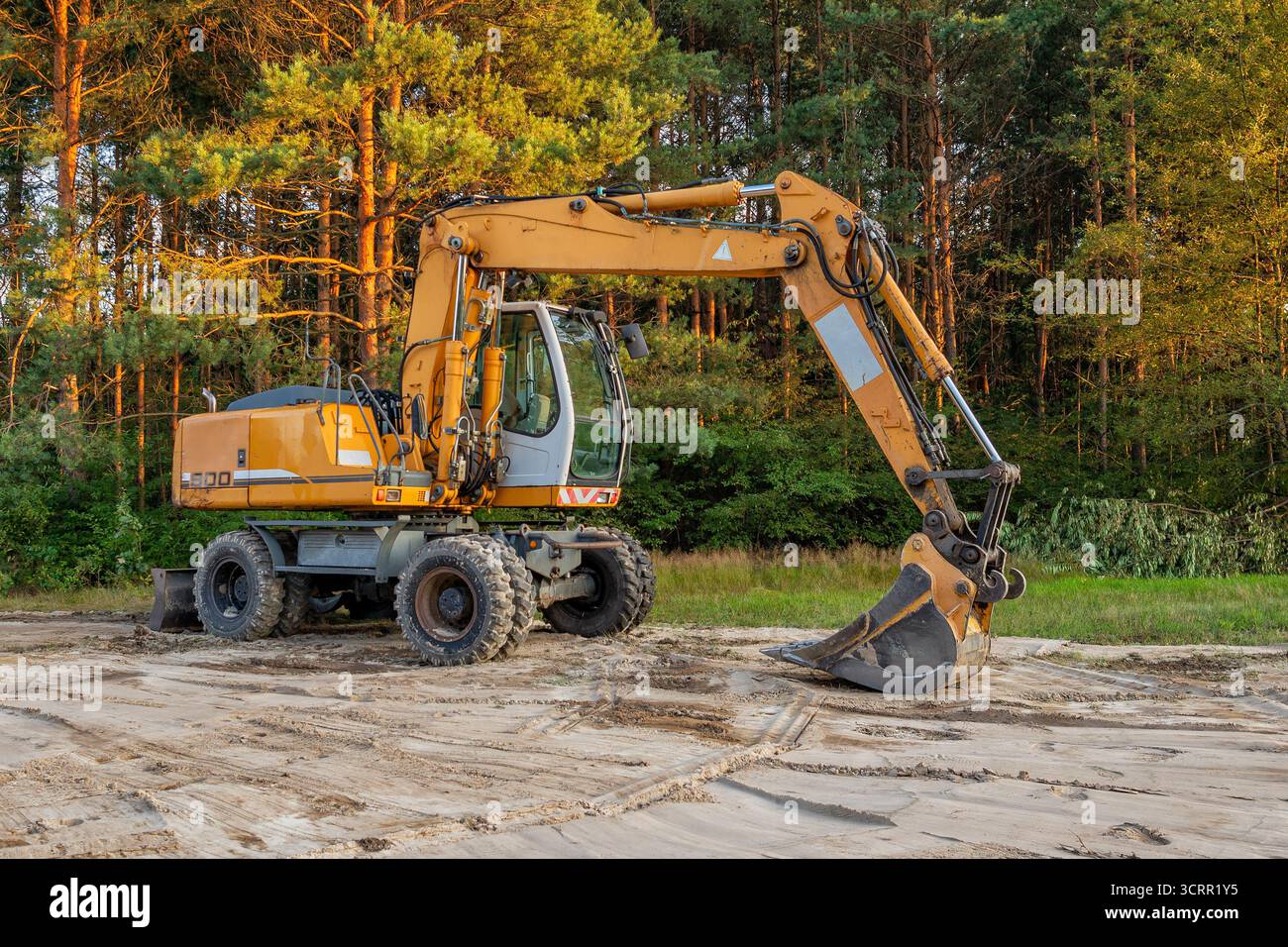 Wheeled excavator levels the sand surface using its bucket to scoop and ...