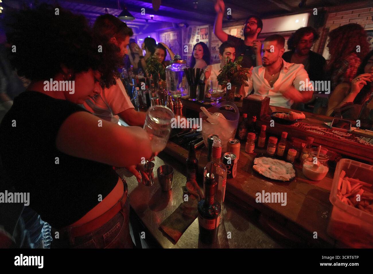 A bartender prepares a drink at a bar, as people enjoy the first night ...