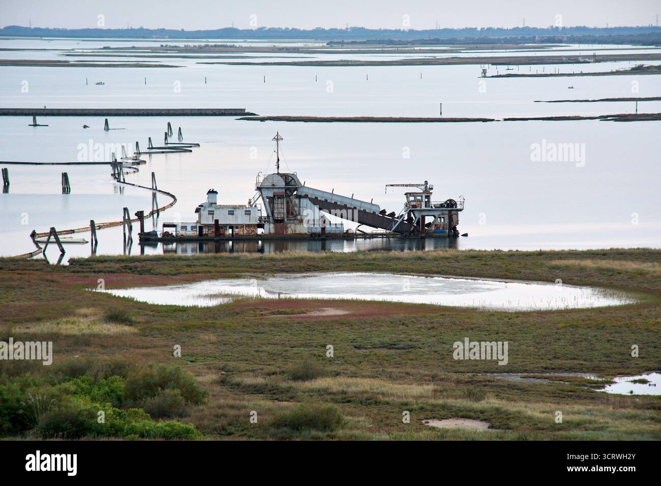 An old industrial dredger is stationary in the shallow waters of a ...