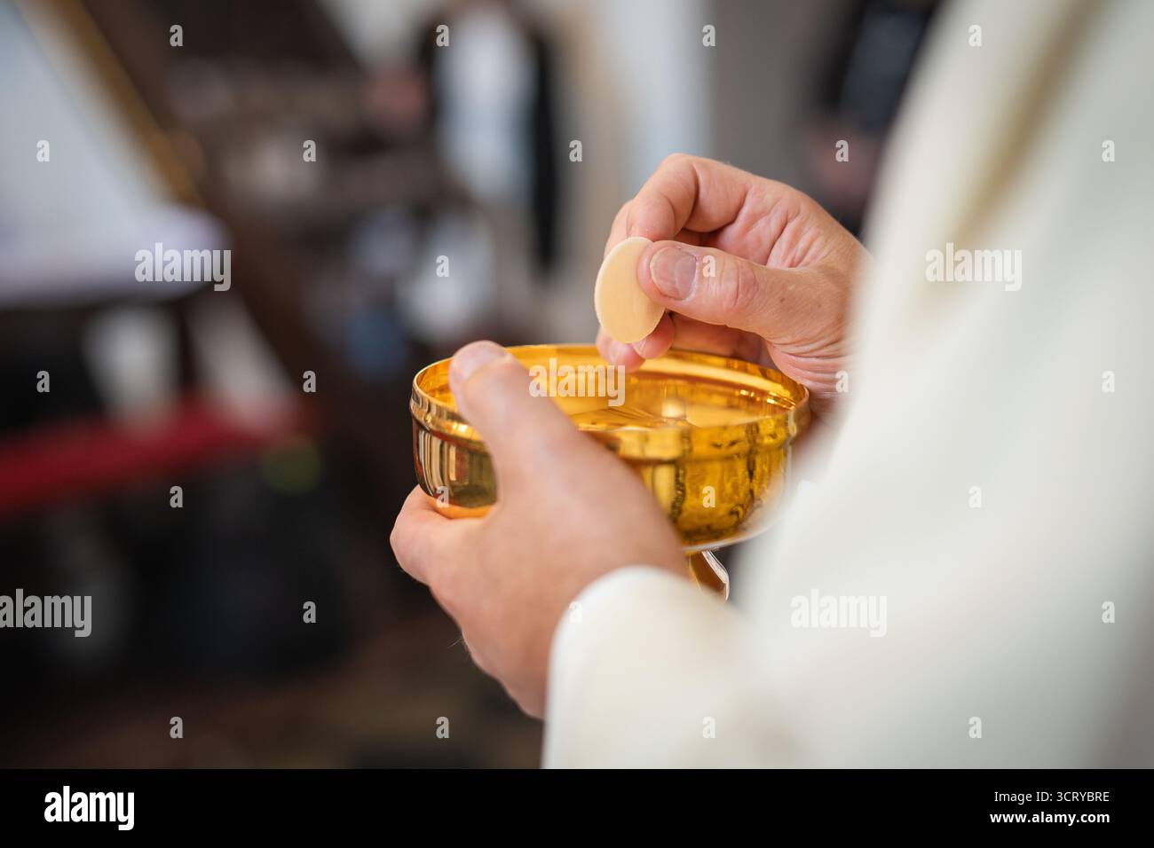 A priest holding a golden chalice and a wafer in his hands while ...