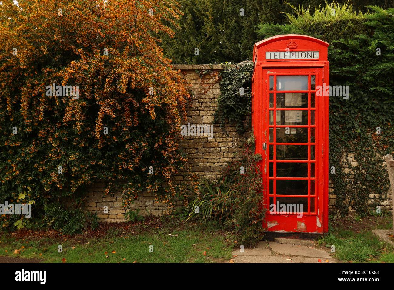 Iconic red British telephone box beside a rustic stone wall, surrounded ...