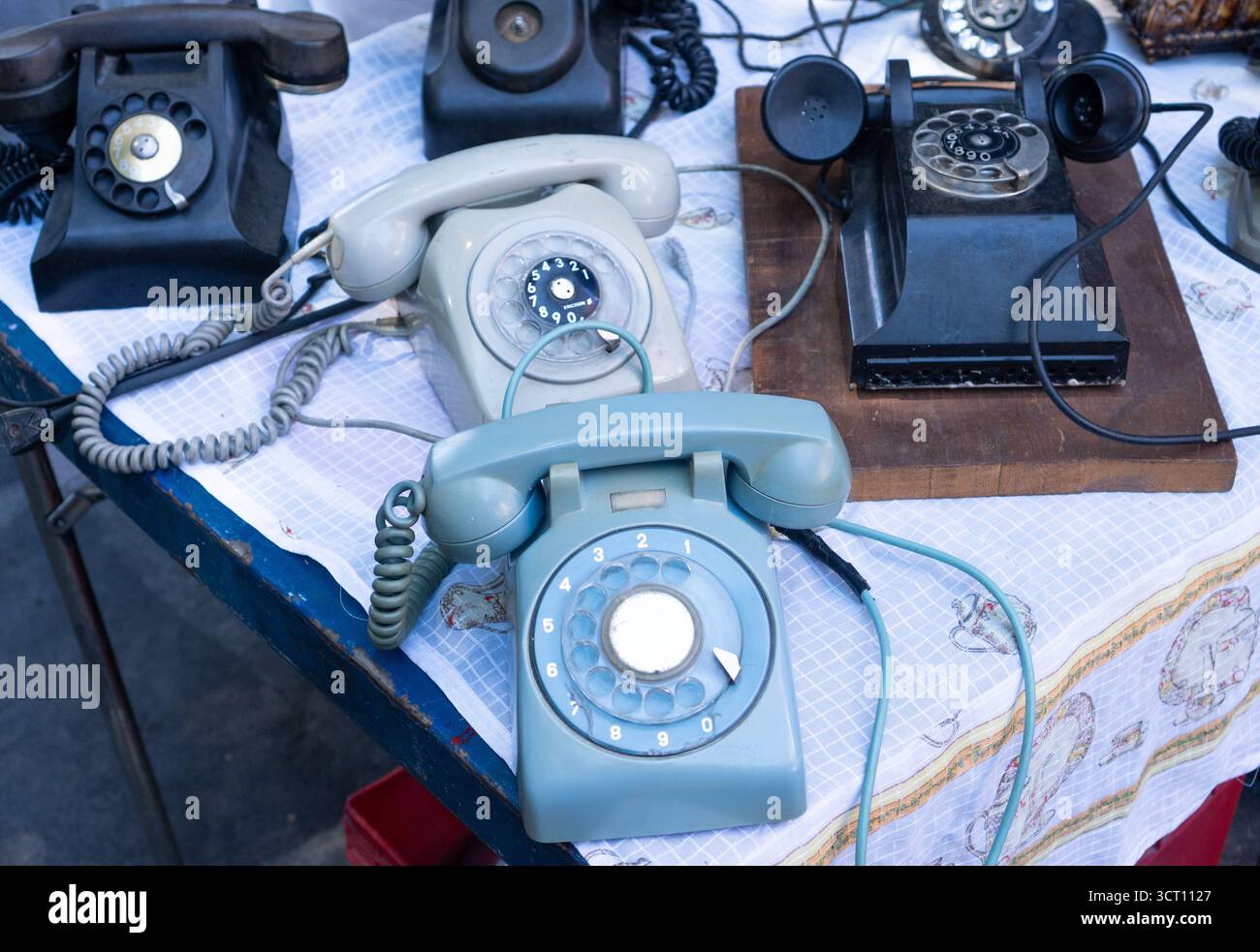 A row of old fashioned phones sit on a table. The phones are of ...