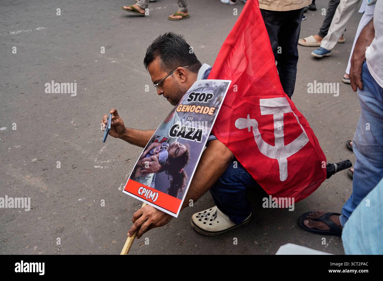 A man holds a poster and a leftist party flag as he takes pictures ...