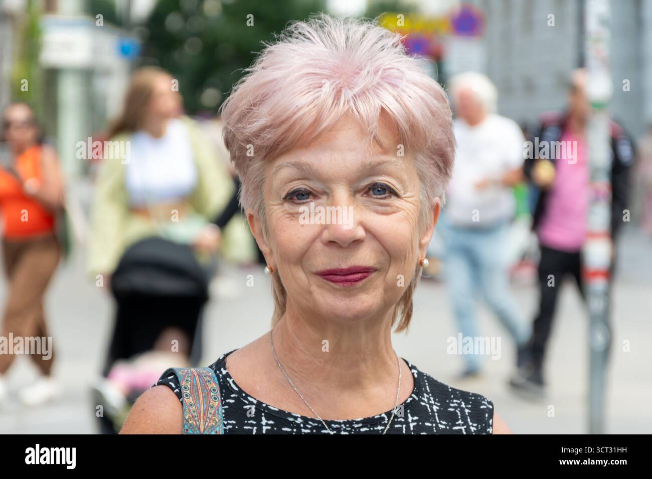 An elderly pensioner, 65-70 years old, with short pink hair smiles on a ...