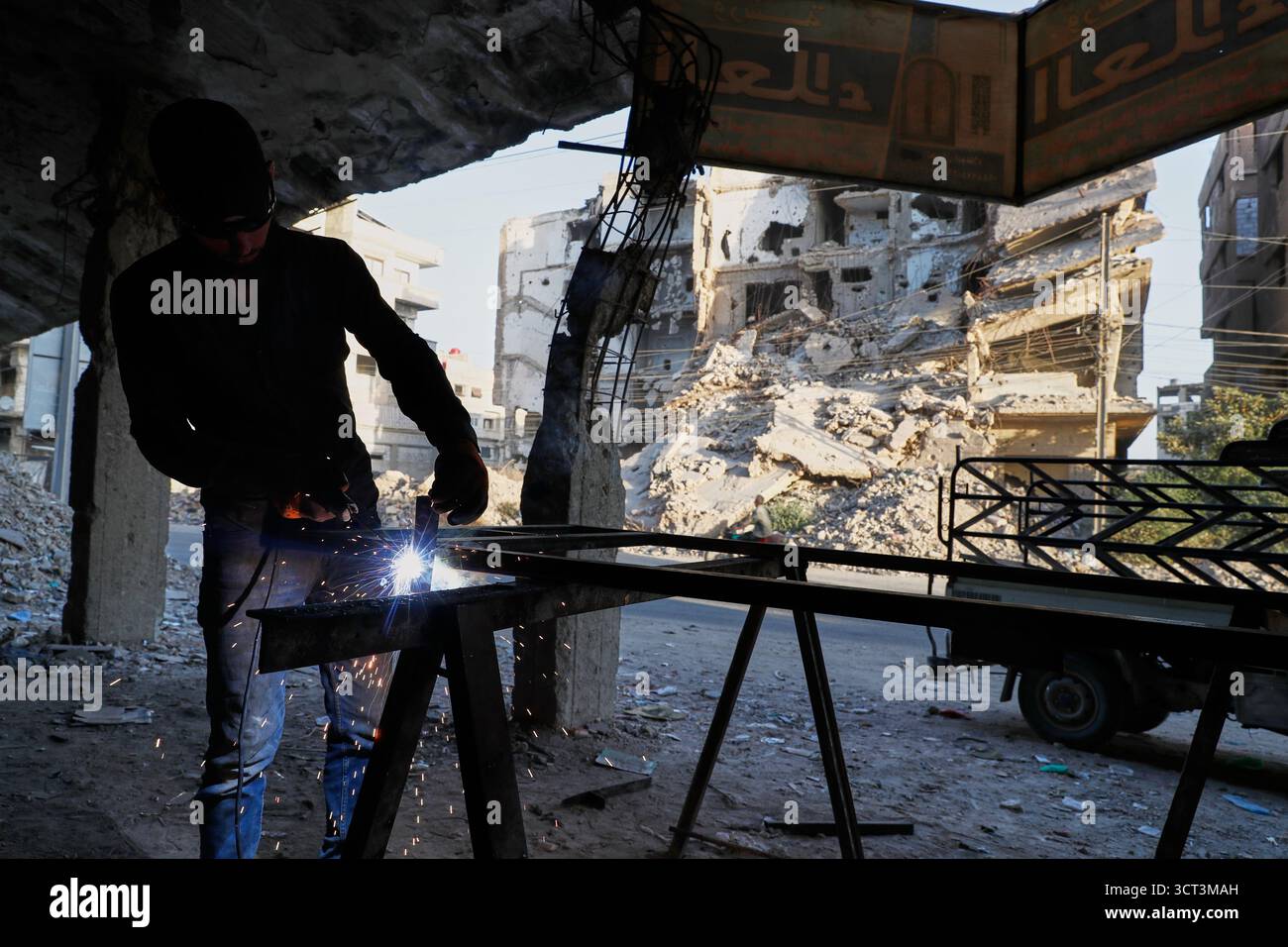 A man welds a frame next to war-damaged buildings in the Damascus ...