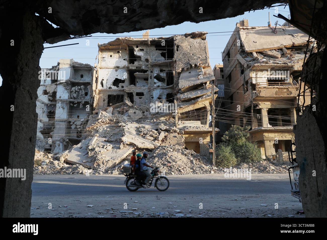 Residents ride a motorcycle past war-damaged buildings in the Damascus ...