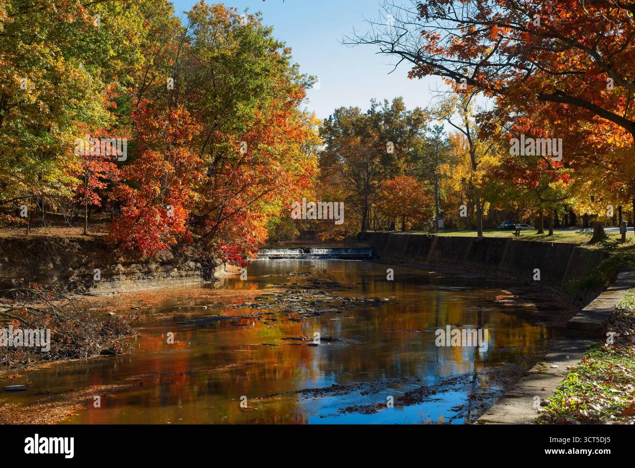 The Rocky River flows over a small spillway amid autumn foliage in ...