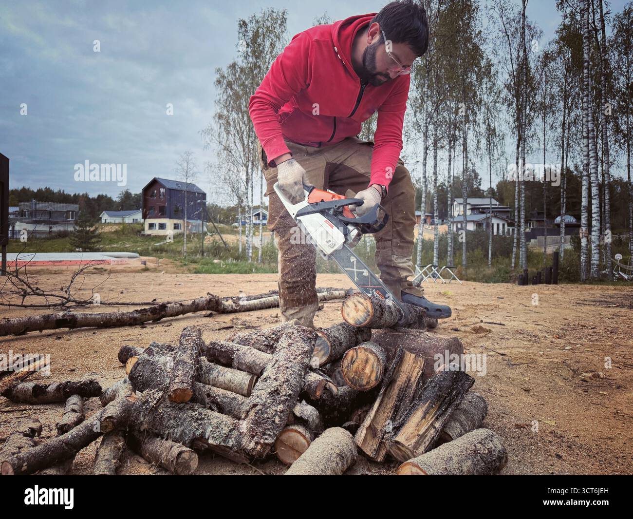 A man cutting a log into firewood using a chainsaw Stock Photo - Alamy