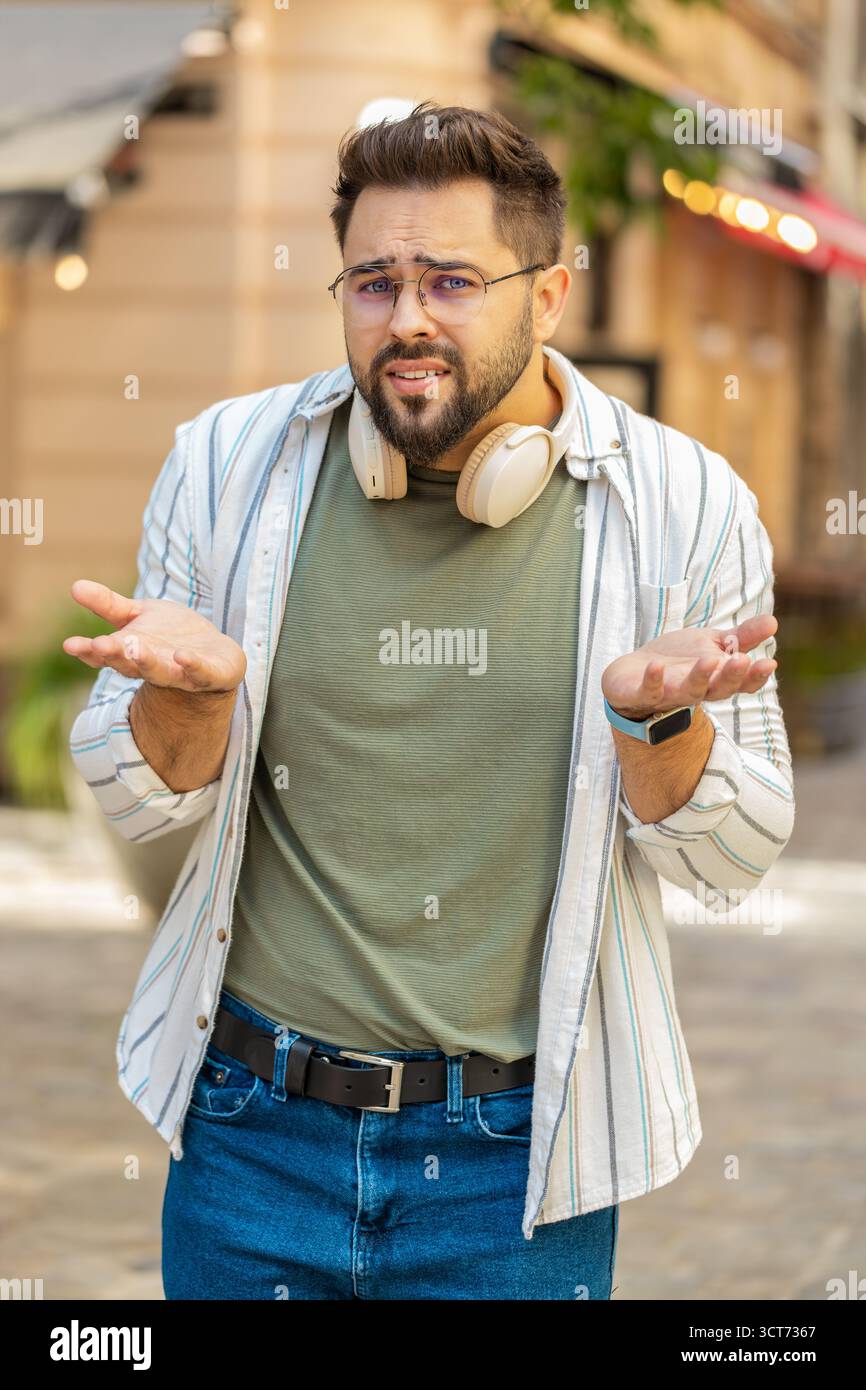 Doubtful sad frustrated young man tourist shrugging shoulders dont know ...