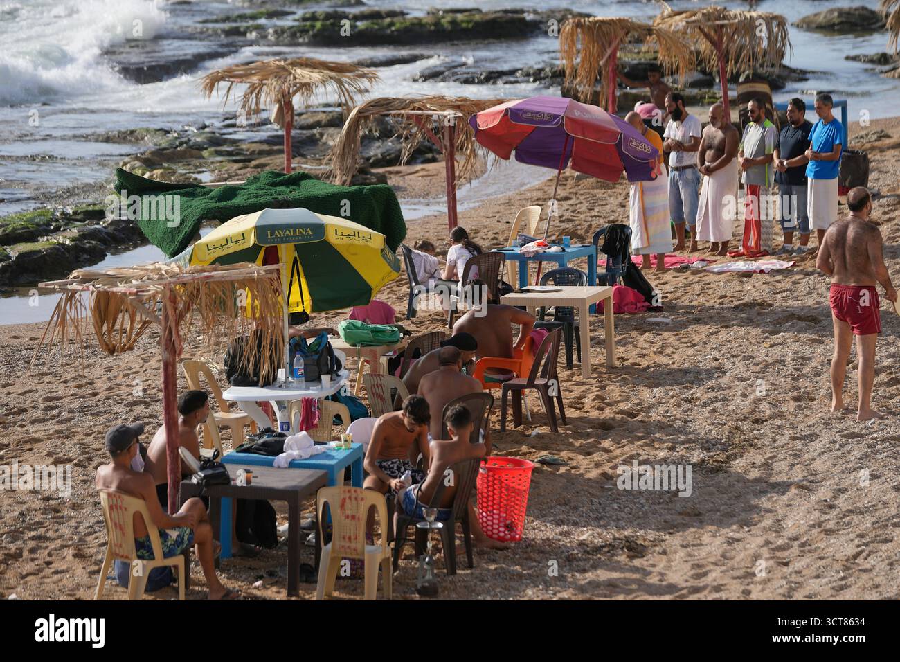 Syrian men attend their noon prayer, background, as others sunbathe at ...