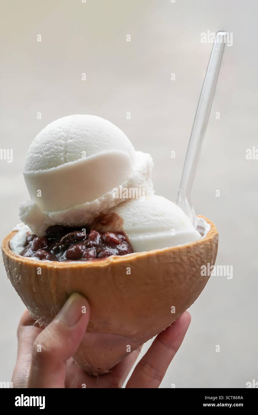 Handheld ice cream sundae in a coconut shell with coconut scoops and ...