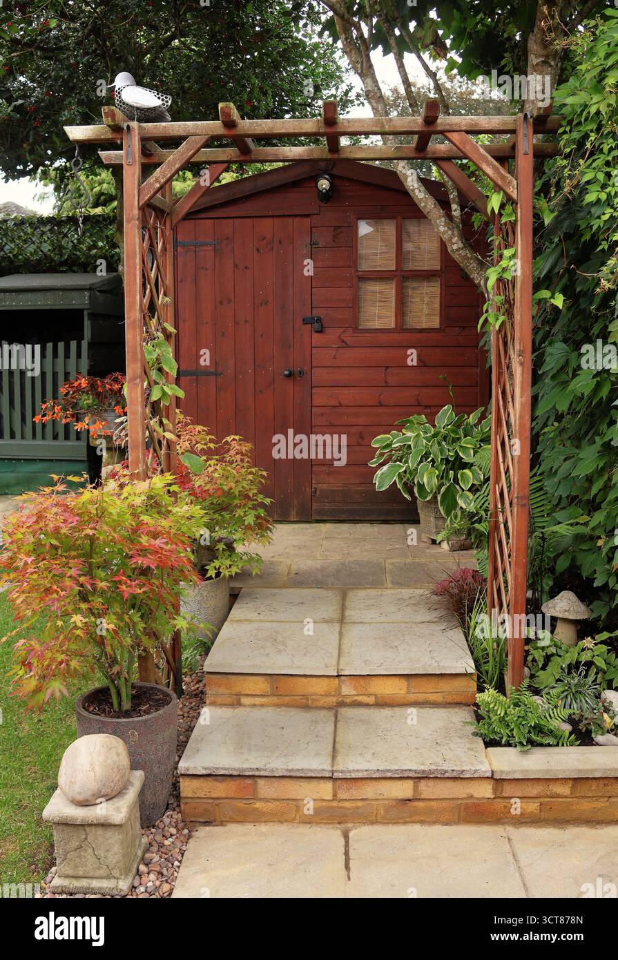 Steps through a wooden arch leading to a garden shed with planters and ...