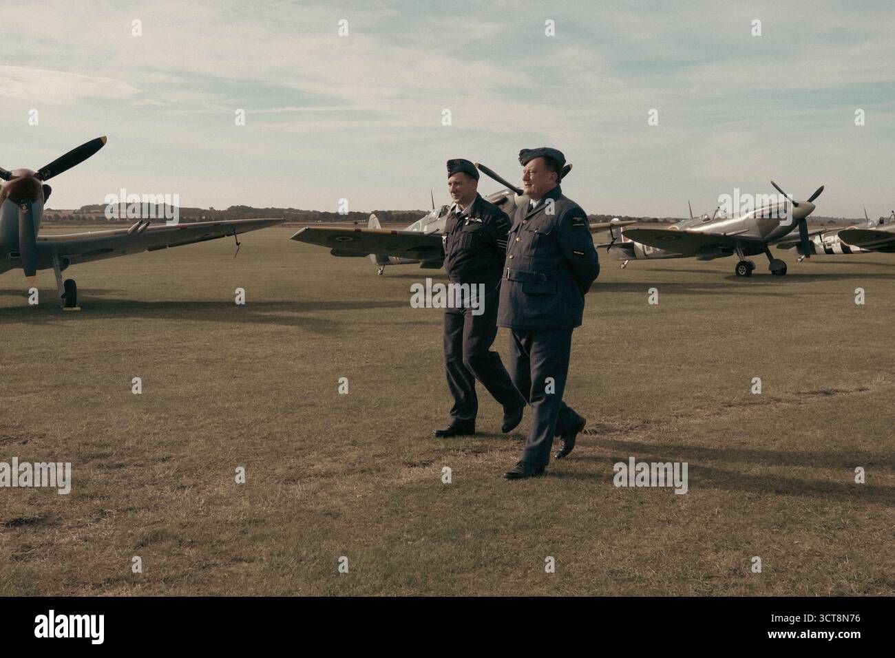 Two RAF pilots walking across airfield with vintage wartime aircraft at ...