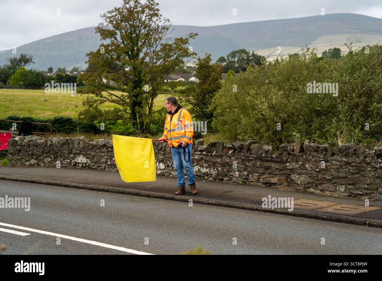 Marshal with yellow flag at Isle of Man road race in scenic countryside ...