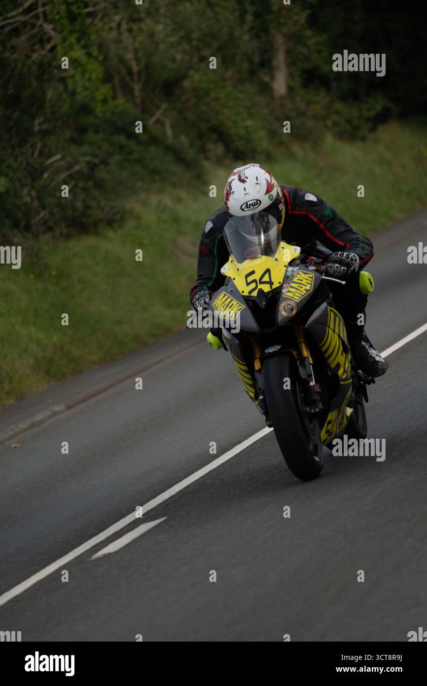 Racing motorcycle number 54 on country road with green foliage backdrop ...