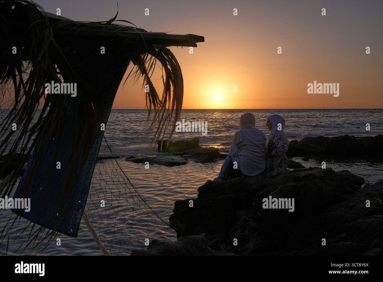 Syrian women sit on a rock enjoying the sunset at a public beach on the ...