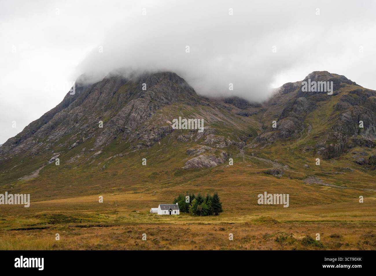 Remote white cottage nestled beneath dramatic cloud-shrouded Scottish ...