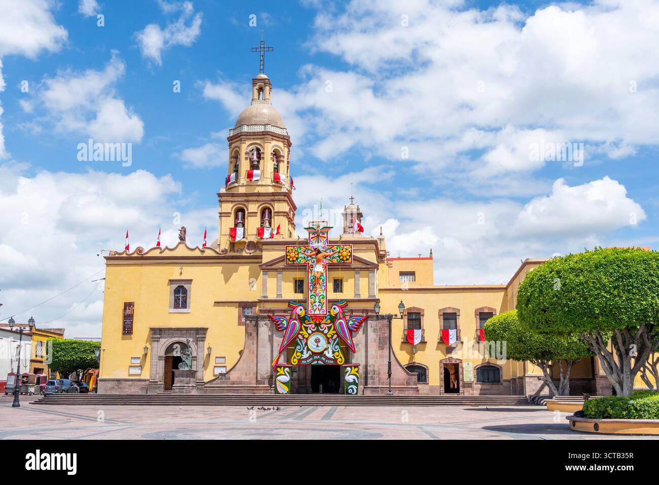 A large yellow building with a tall tower and a cross on top. The ...