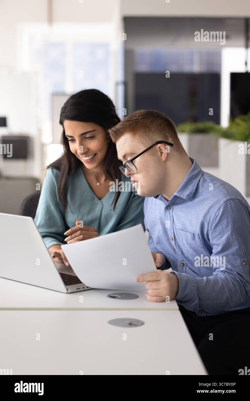 Positive professional woman giving help to employee with Down syndrome ...