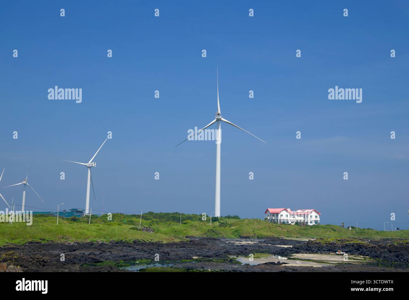 A large wind turbine stands above basalt reefs and a hillside ...
