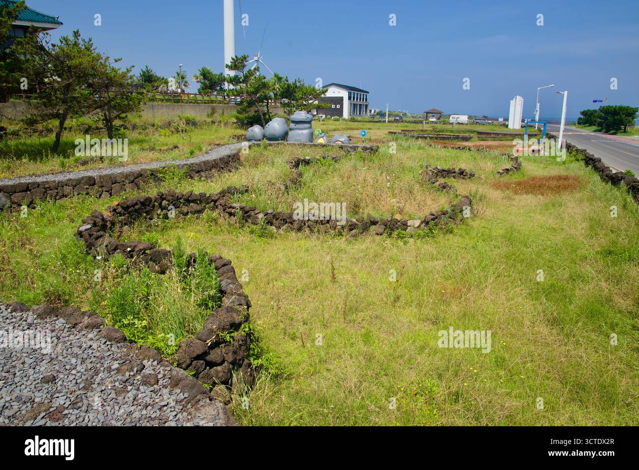 Sinuous Batdam dry‑stone walls curl across grassy plots beside a gravel ...