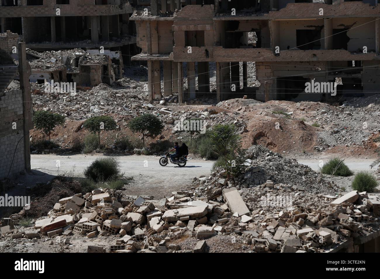 A couple rides a motorcycle past destroyed buildings in Ein Tarma ...