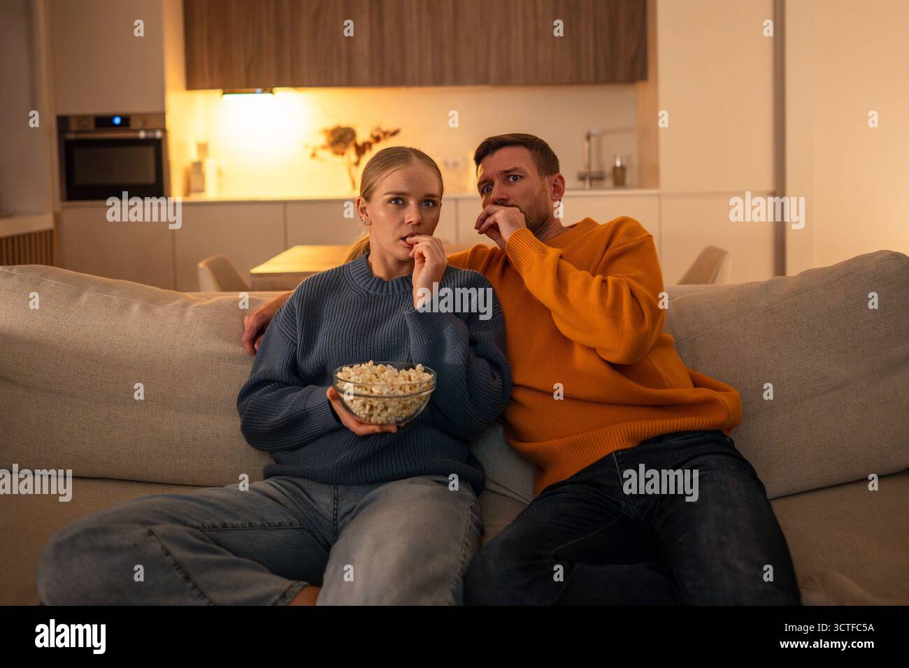 Fearful shocked couple watch thriller movie with popcorn at home ...