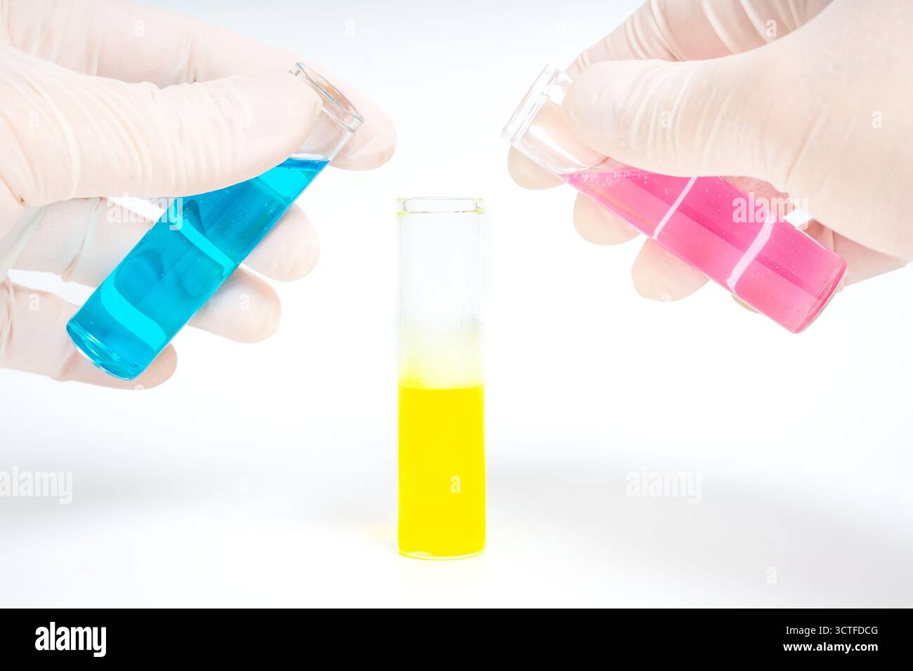 Gloved hands holding glass test tubes with blue, pink and yellow ...