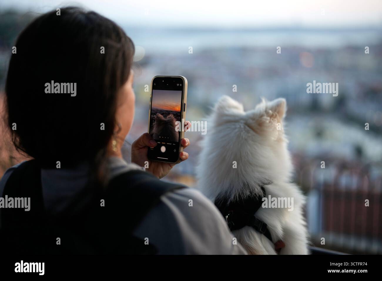 A woman takes pictures of the sunset while holding a dog, at the Our ...