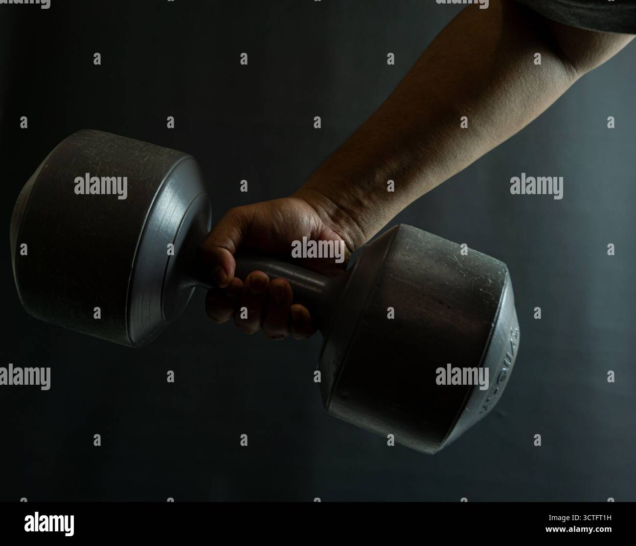 Hand lifting cement-filled plastic dumbbell above white surface ...