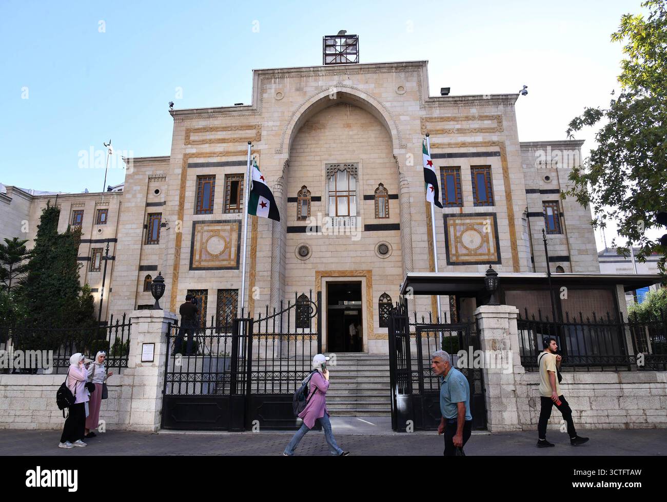 Damascus, Syria. 6th Oct, 2025. People pass in front of the Syrian ...