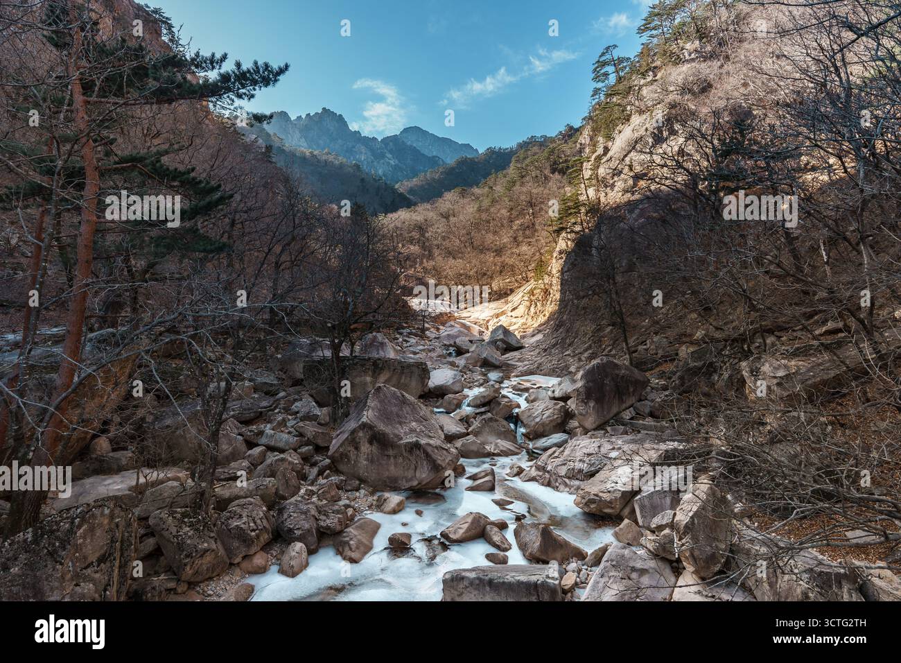 A partially frozen stream winds through a rocky valley surrounded by ...