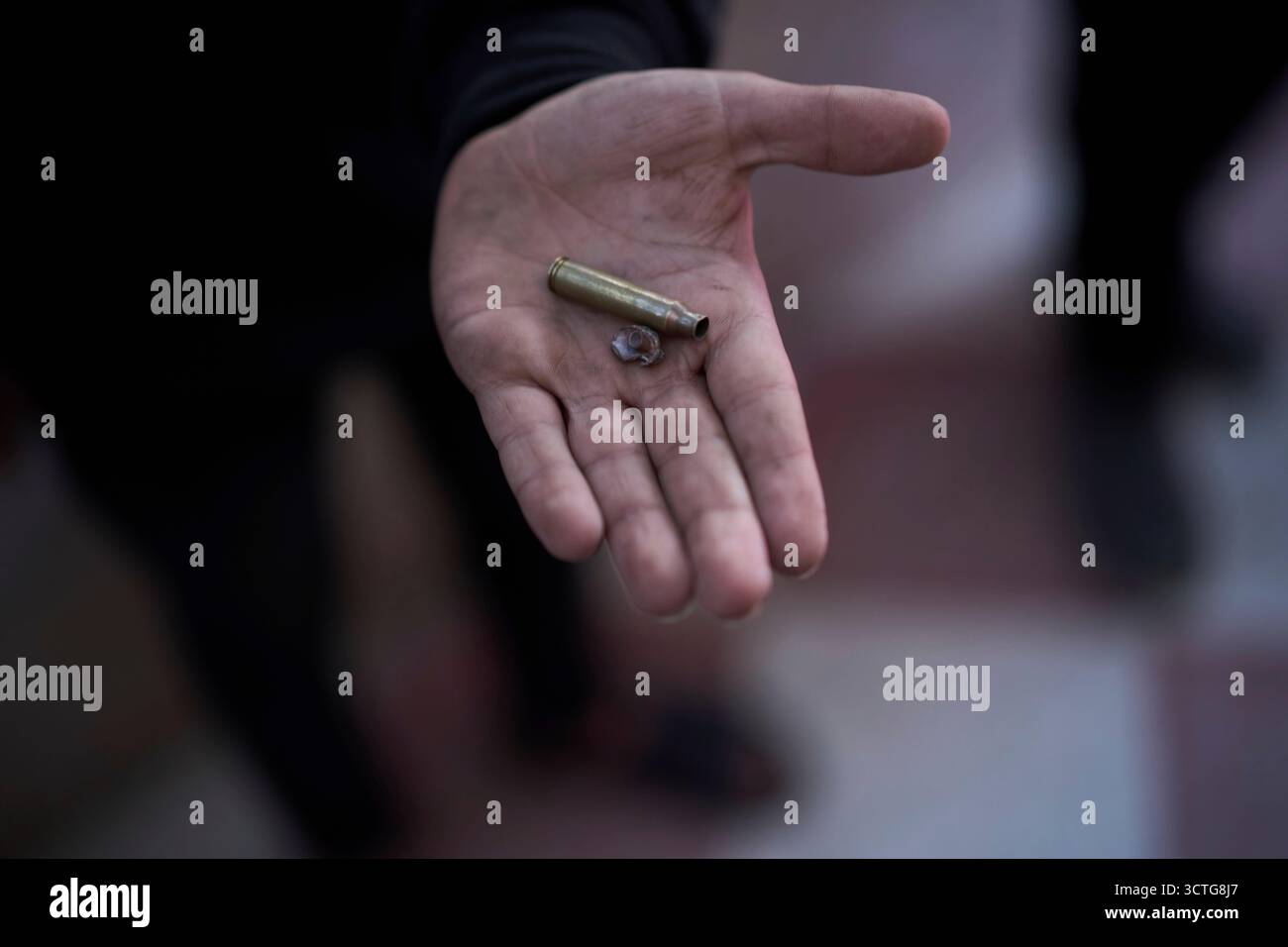 A youth holds an empty bullet cartridge and a piece of shrapnel near ...