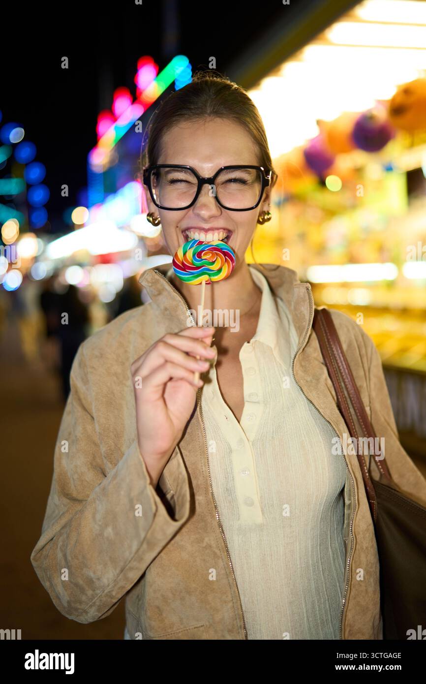 Happy woman enjoying colorful lollipop at night fair Stock Photo - Alamy