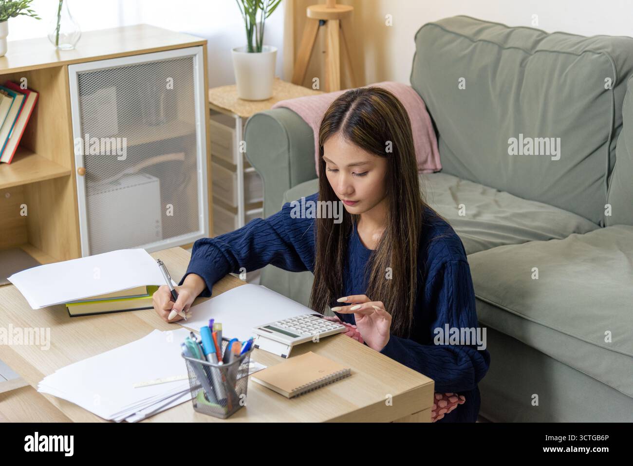 Teen girl student doing homework, writing, using calculator for school ...
