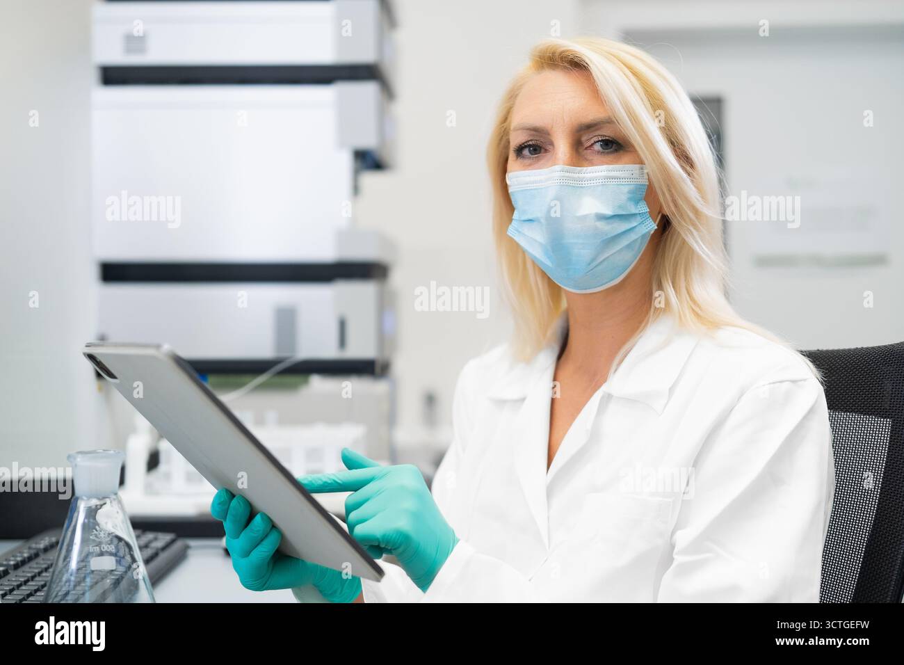 Blonde female scientist wearing a mask and rubber gloves recording ...