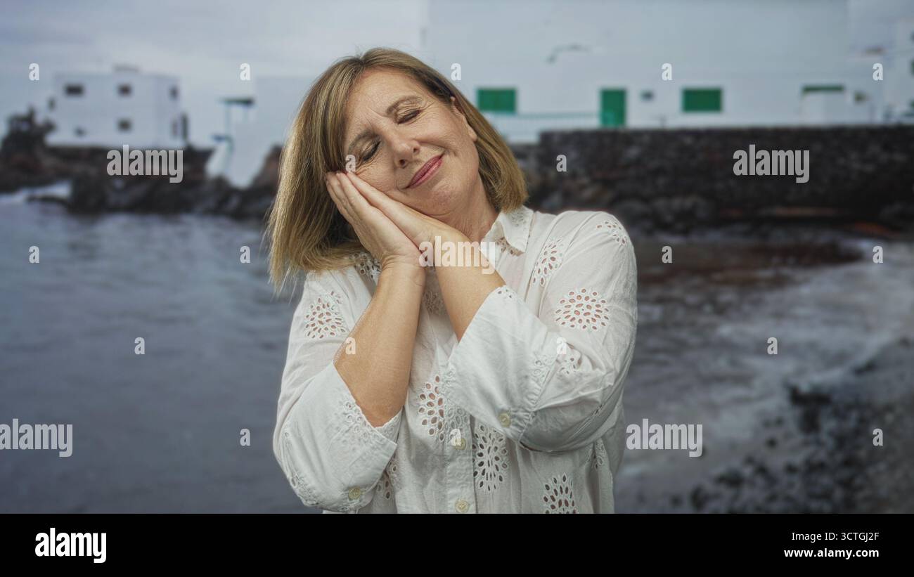 Woman places cheek on hands in a sleeping gesture by the seaside with ...