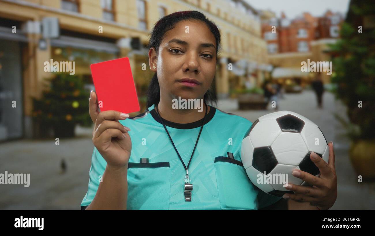 Woman referee holding red card and soccer ball on busy street in view ...