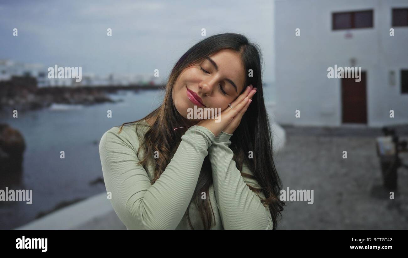 Young hispanic woman makes sleeping gesture with hands under cheek ...