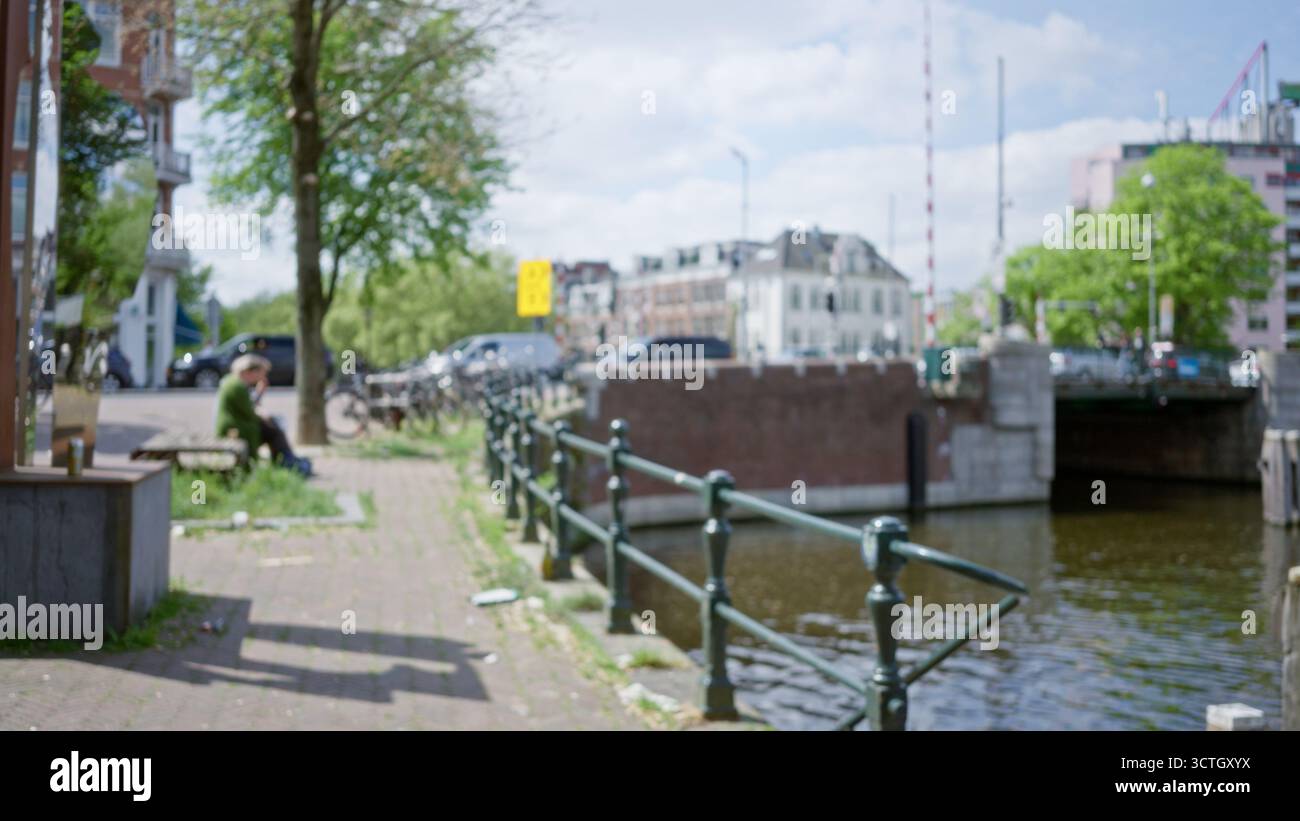 Blurred man in green sweater sits on canal bench in amsterdam with ...