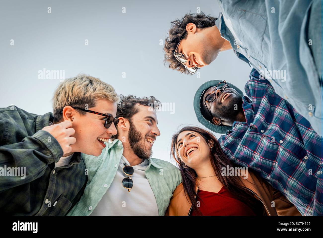 From a low angle, a happy group of young diverse friends huddles in a ...