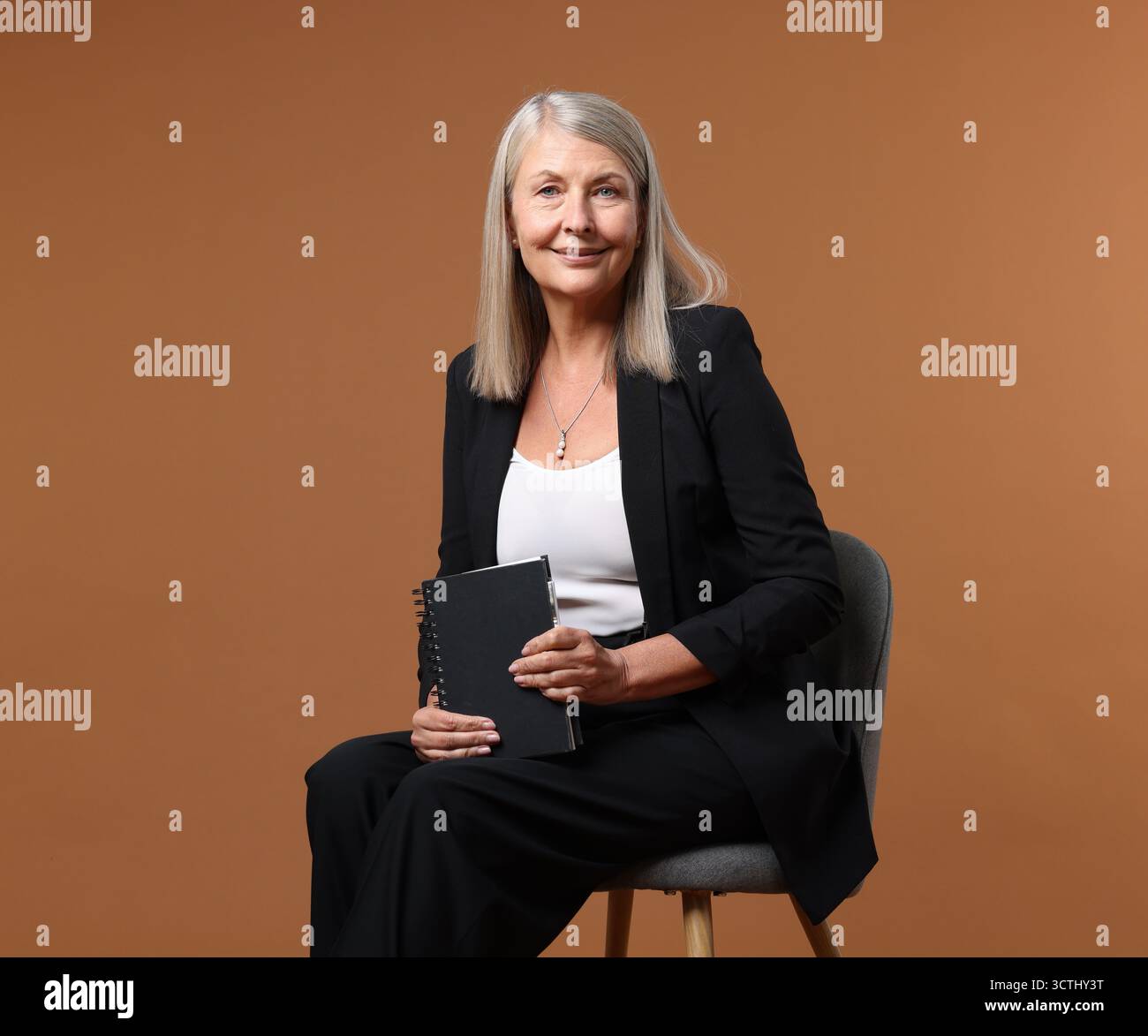 Professional psychotherapist with notebook on chair against brown ...