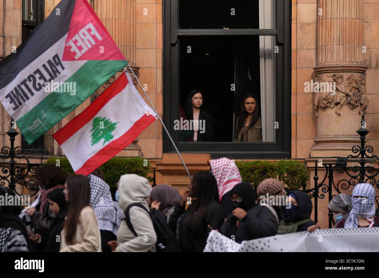 Guests look out from a hotel window as students demonstrate holding ...