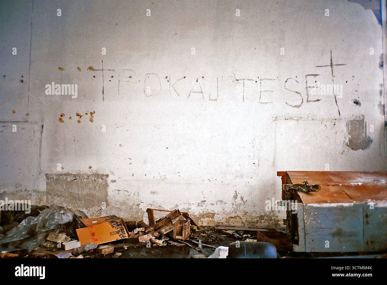 White crumbling factory walls with graffiti “Rokaj te se” and a cross ...