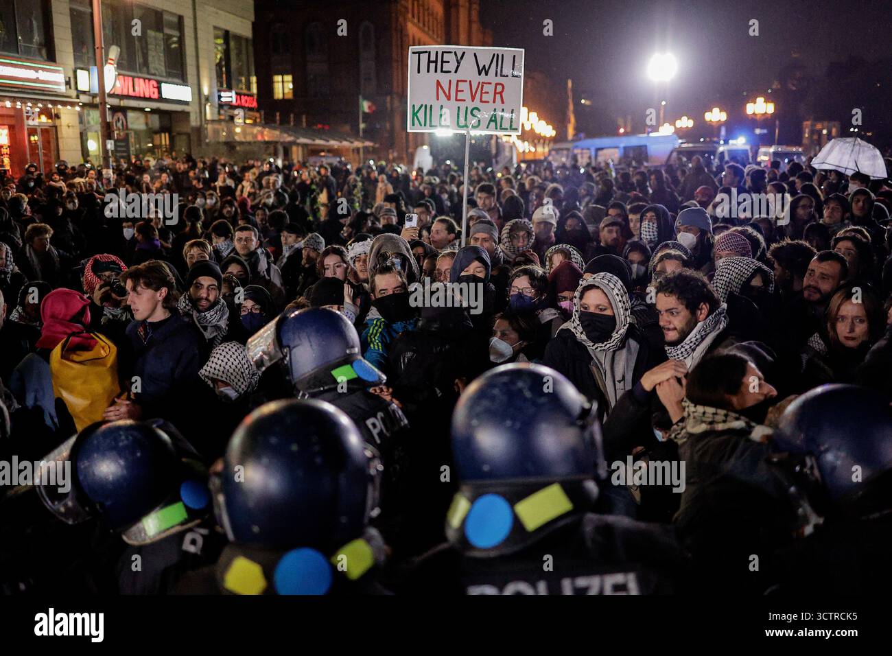Protesters stand in front of police officers holding a placard saying ...