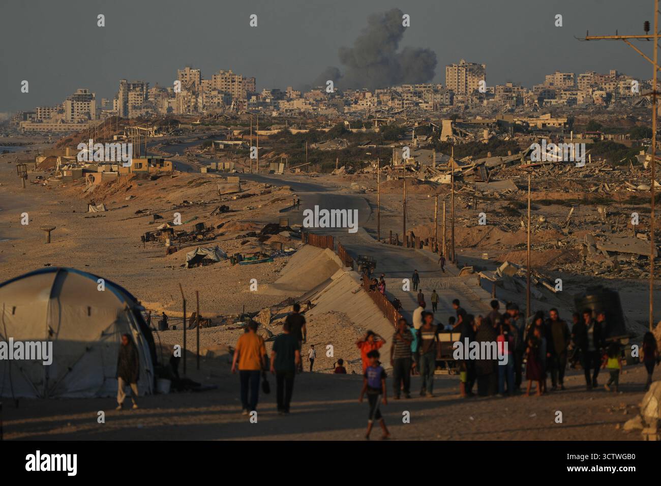 Displaced Palestinians walk along the coastal road, backdropped by ...