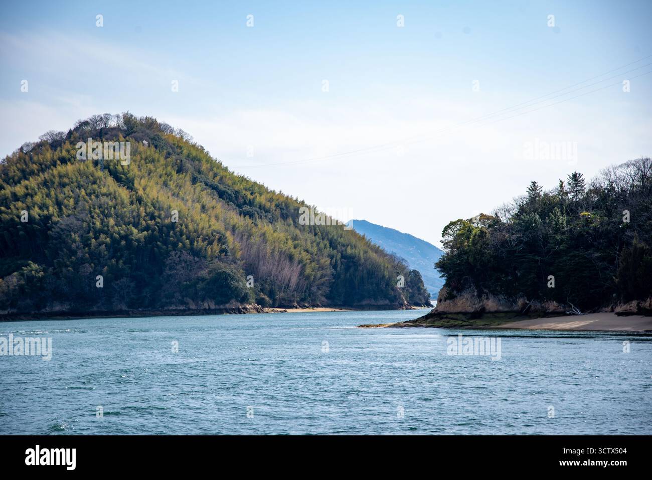 A scenic narrow waterway flowing between two lush green coastal hills ...
