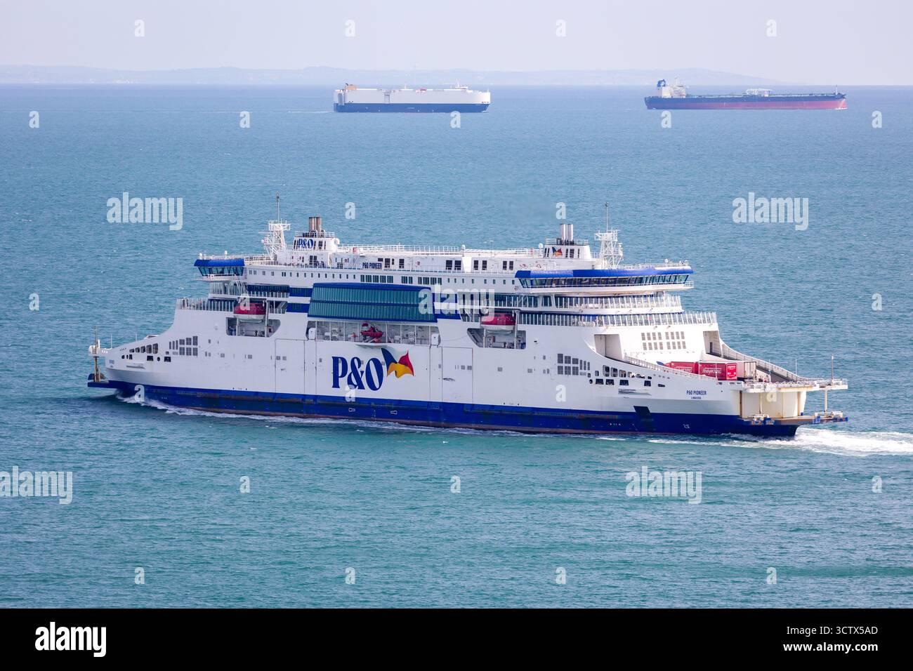 Ferry departing the Port of Dover on a hazy day with cargo ships in the ...
